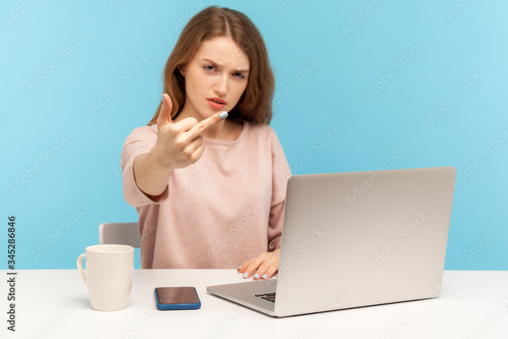 Impolite furious young woman employee sitting at workplace with laptop ...