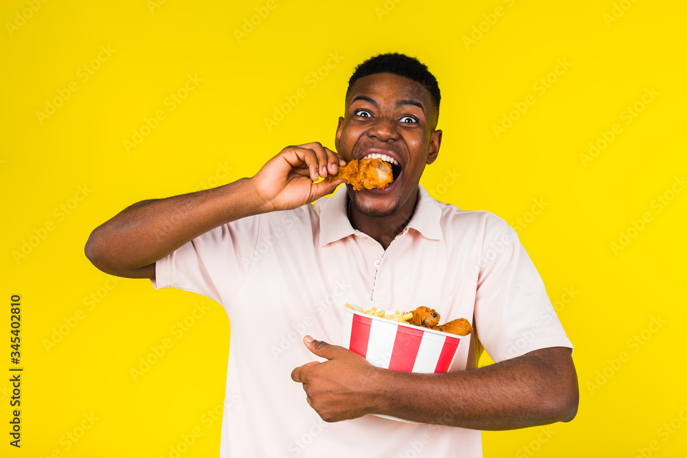 African American young guy eats fast food, chicken leg and a whole ...
