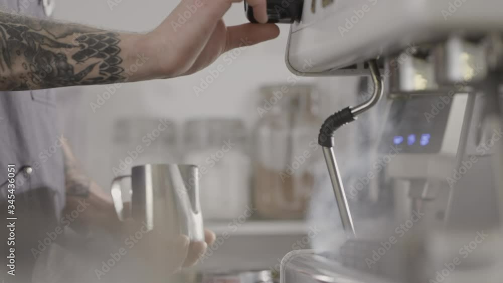 Barista hands makes steam in the coffee machine and whips the milk in ...