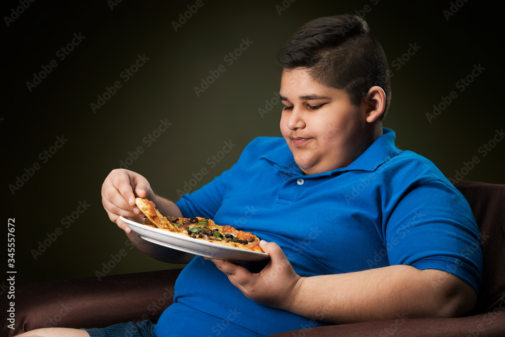Young boy sitting on the sofa and with a pizza in his hand. (Obesity ...