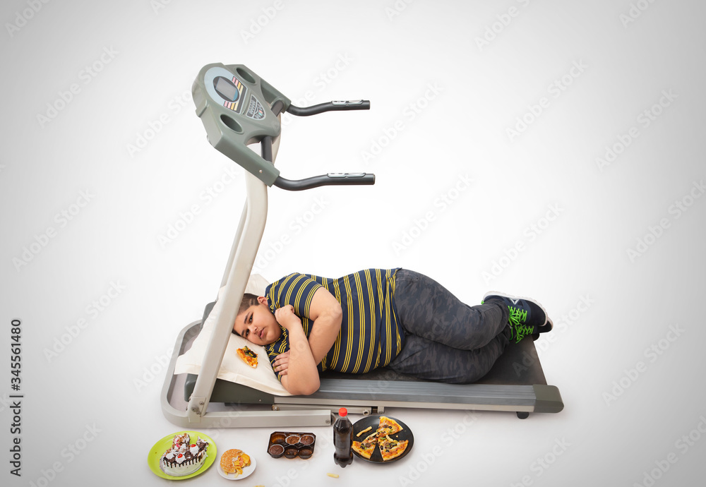 Young boy sleeping on the treadmill with lots of junk food around him ...