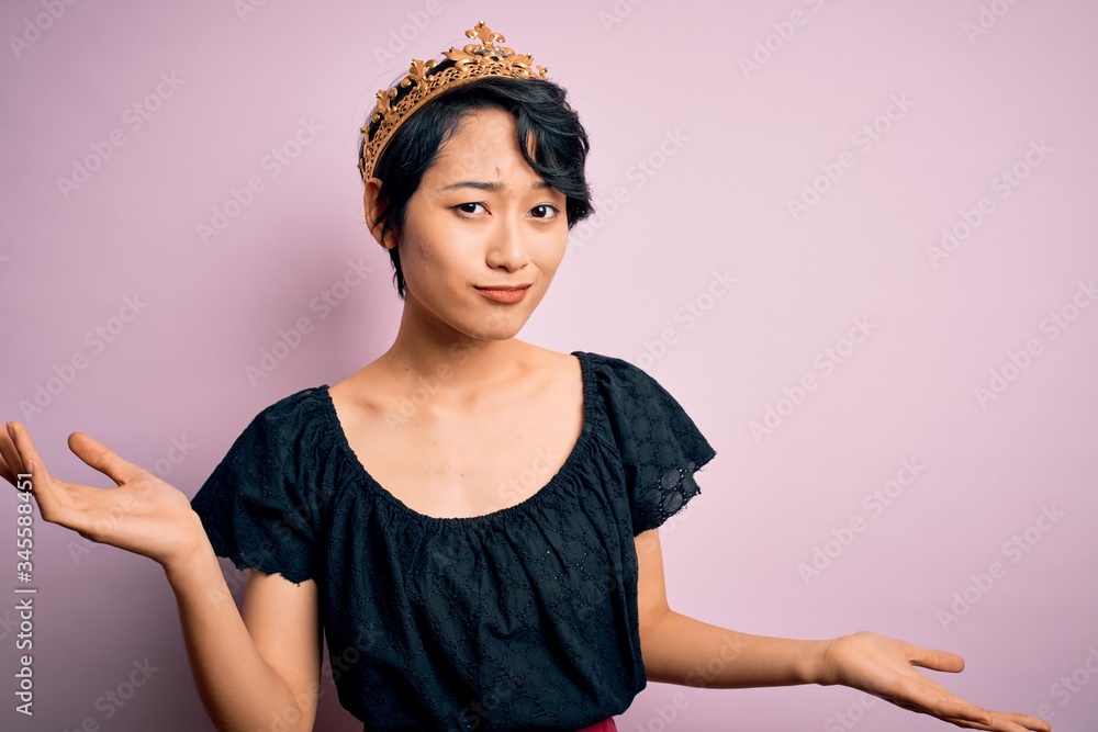 Young beautiful chinese woman wearing golden crown of king over ...