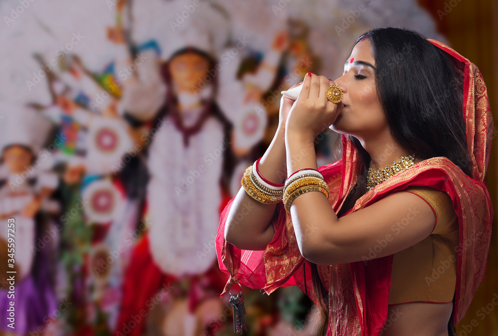 Portrait of a beautiful Bengali woman blowing conch shell at Durga puja ...