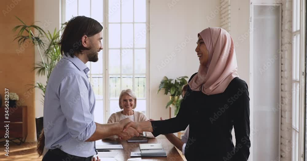 Happy young bearded manager shaking hands with smiling asian arab ...
