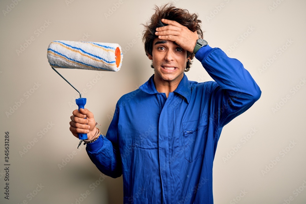 Young handsome painter man holding roller wearing uniform over isolated ...