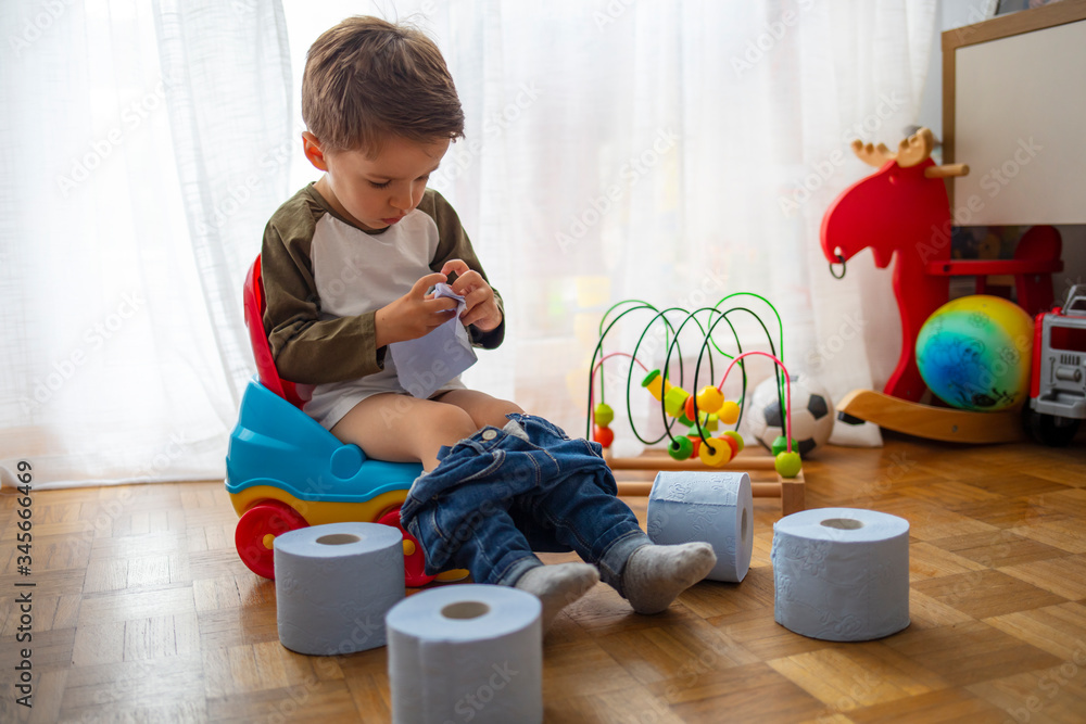Little toddler boy, sitting on potty, playing with toilet paper ...