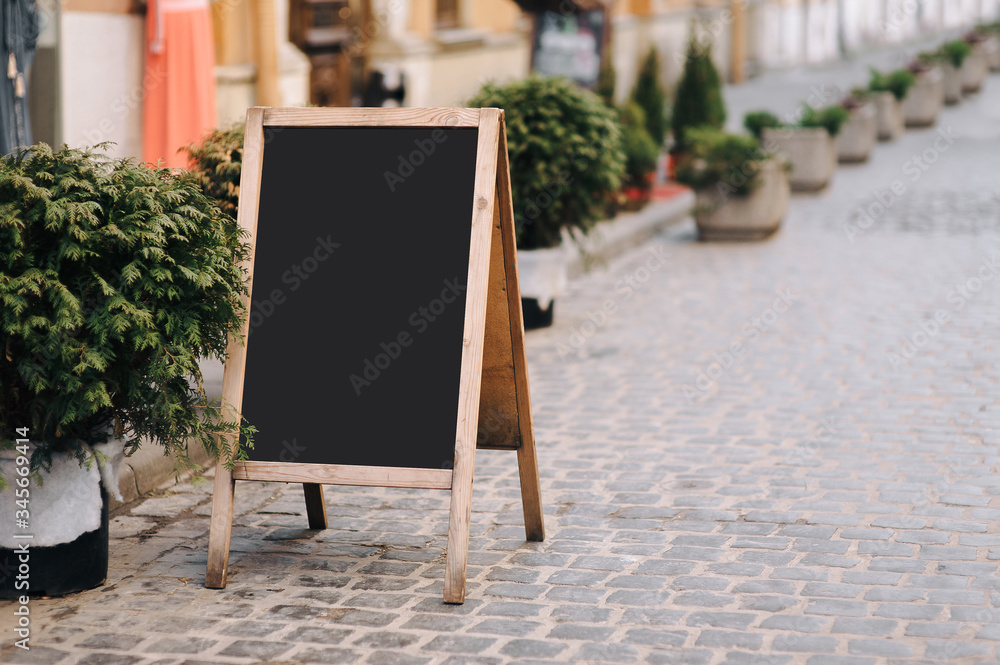 An old black wooden billboard stands on a pavers stones. Outdoor ...