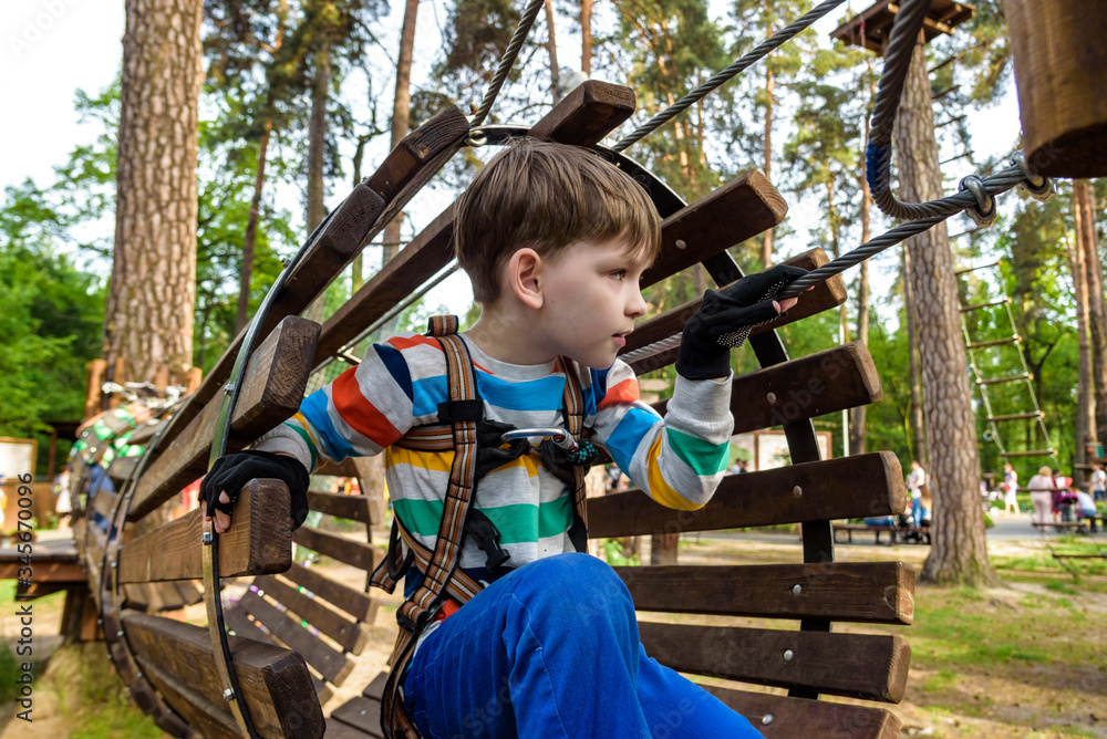 Happy kid overcomes obstacles in rope adventure park. Summer holidays ...