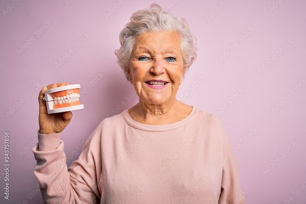Senior beautiful grey-haired woman holding plastic denture teeth over ...