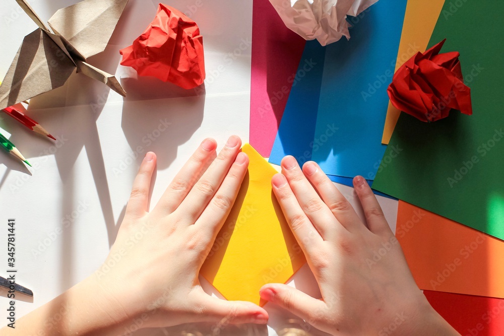 Children’s hands doing origami crane from yellow paper on white ...