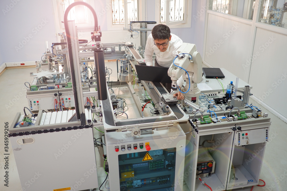 Close-up robot arm. Engineer is working on laptop to programming smart factory automation and ...