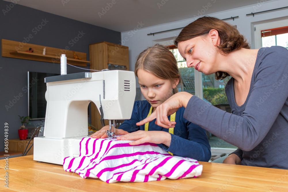 Mother teaches her 8 year old daughter how to sew a striped fabics with ...