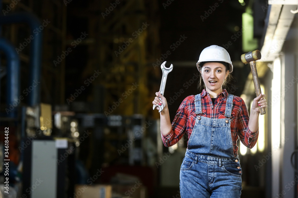 Young girl in a work dress and white hard hat holding big wrench and ...