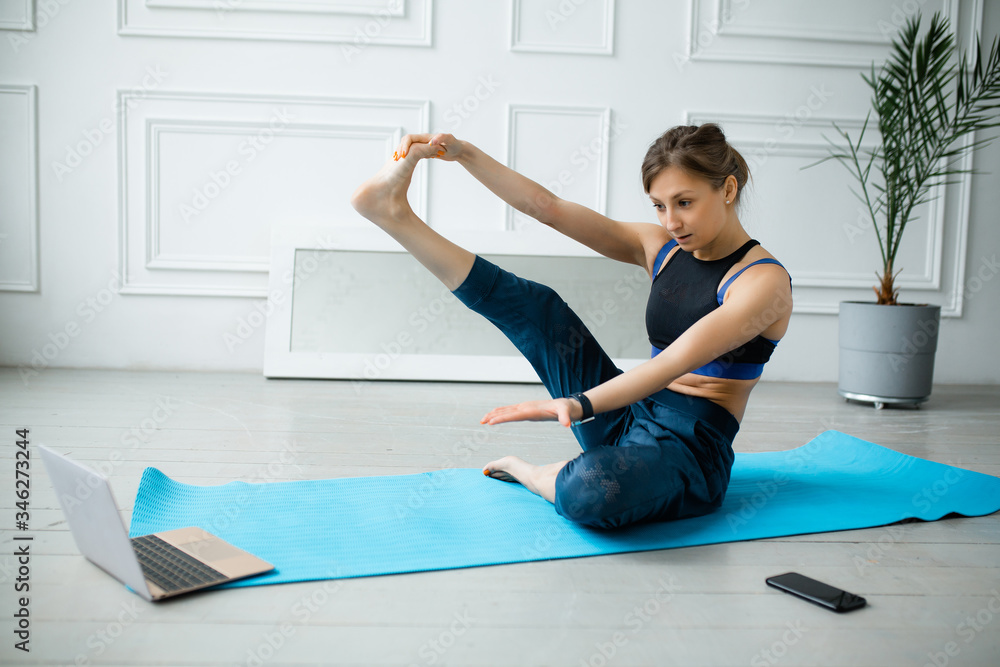 Beginner girl is trying to do new Pilates exercises in a video tutorial ...