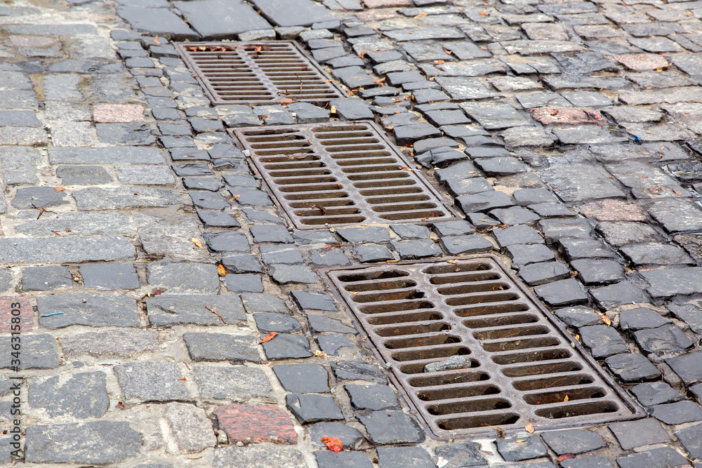 hardscape sett road with iron grate of the drainage system hatch on the ...