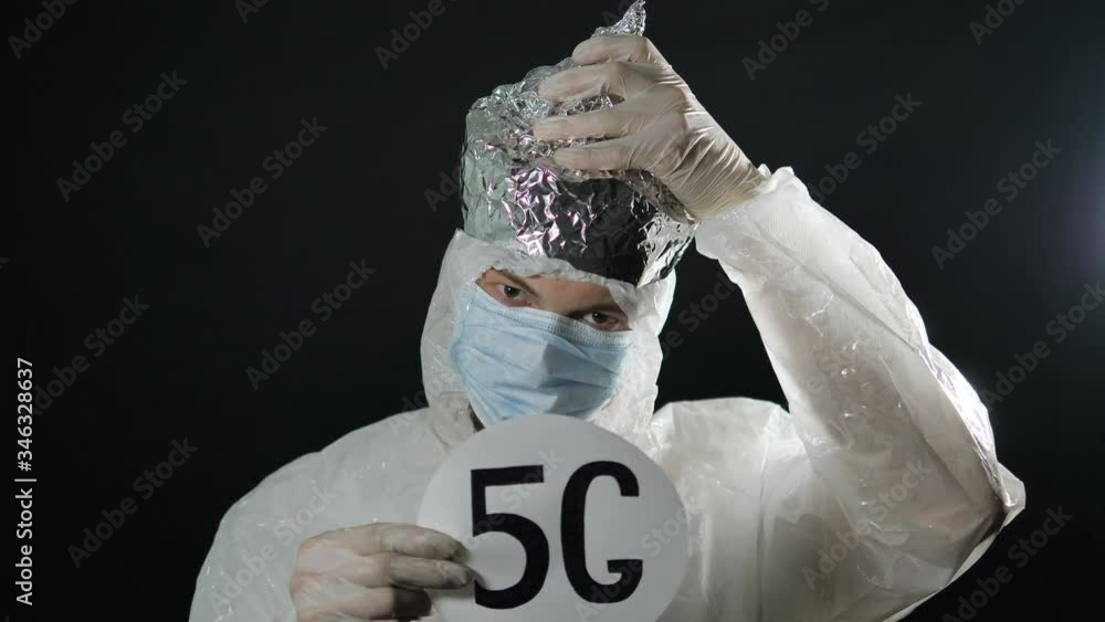 man in a protective suit from coronovirus puts on hat of aluminum foil ...