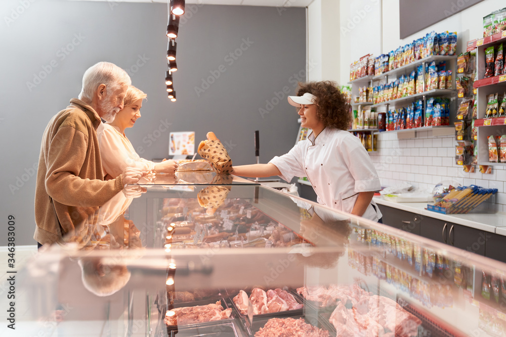 Female butcher giving eldery man with wife sausages. Stock Photo ...