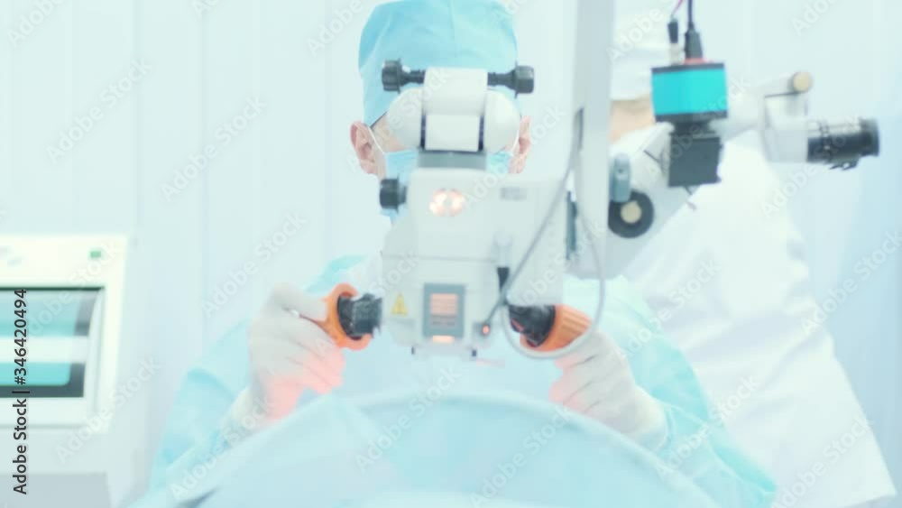 Surgeon looking into the microscope at the eye of female patient at the ...