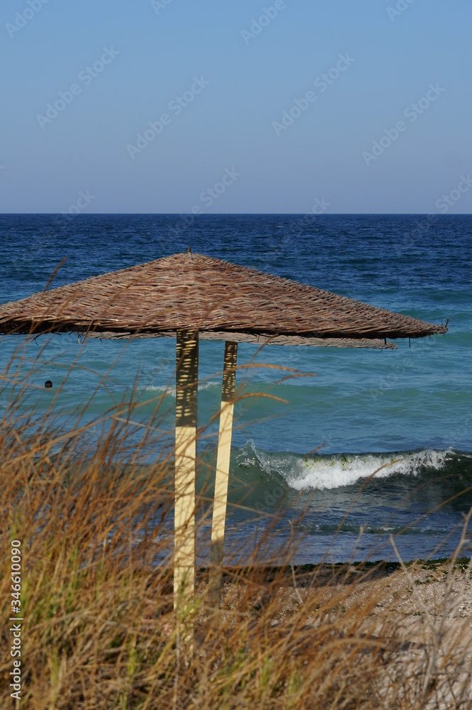 Seaside scene with two wattle parasols on the beach and foamy wave on ...