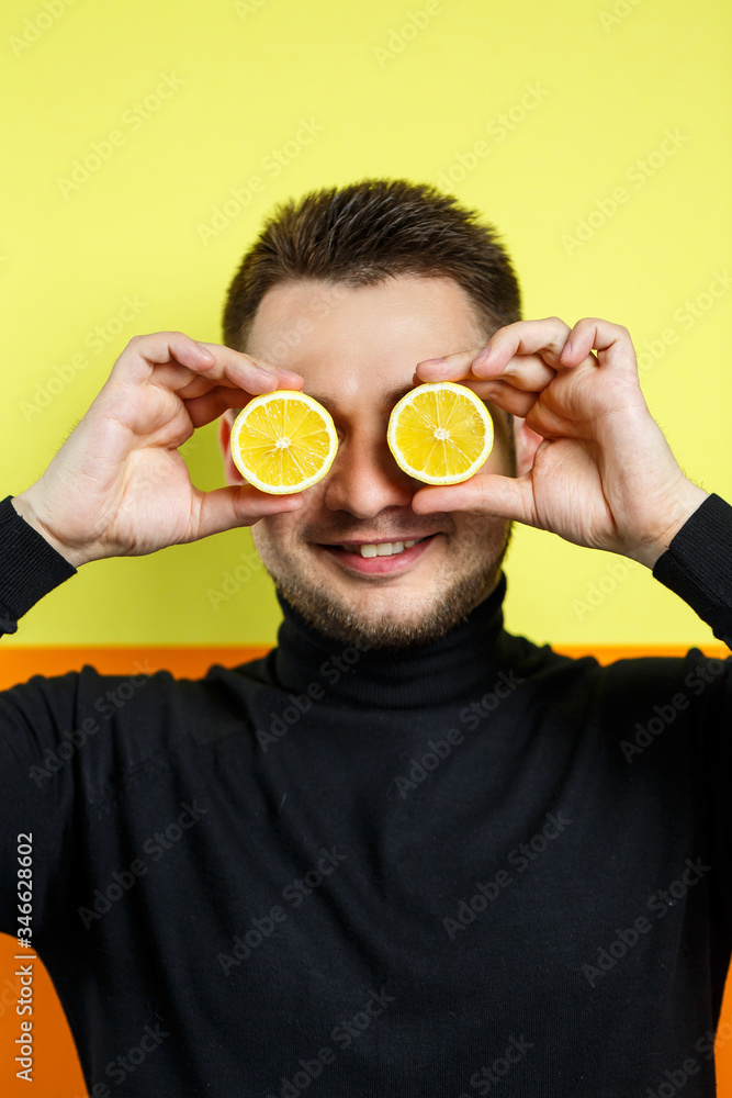 Portrait of a man on a yellow background in black raglan with cut lemon ...