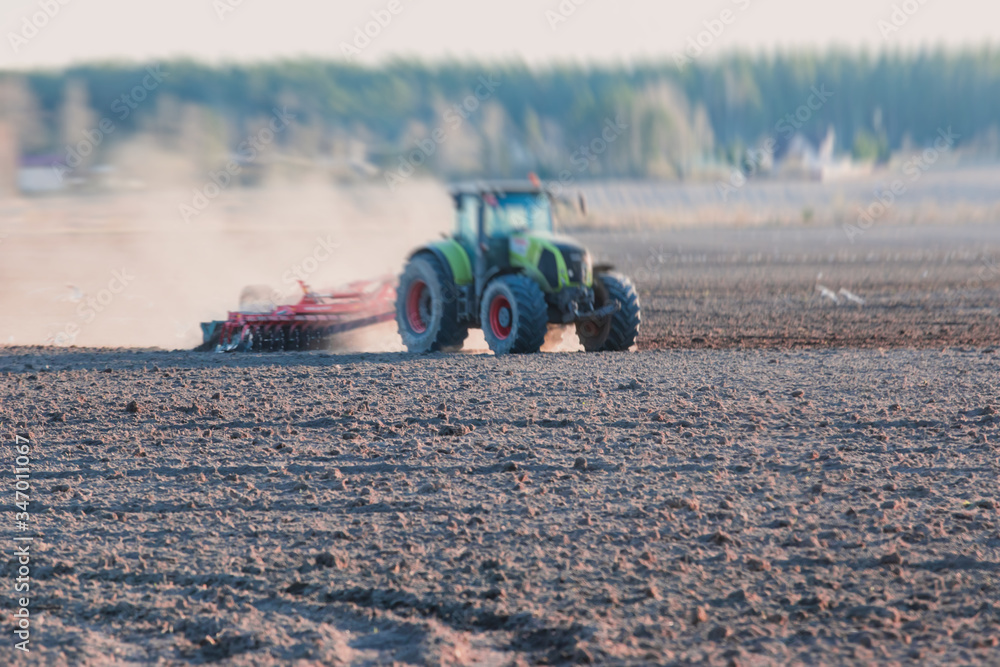 Tractor with a disc harrow system harrows the cultivated farm field ...