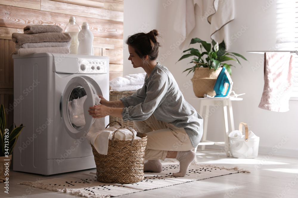 Young woman taking laundry out of washing machine at home Stock Photo ...