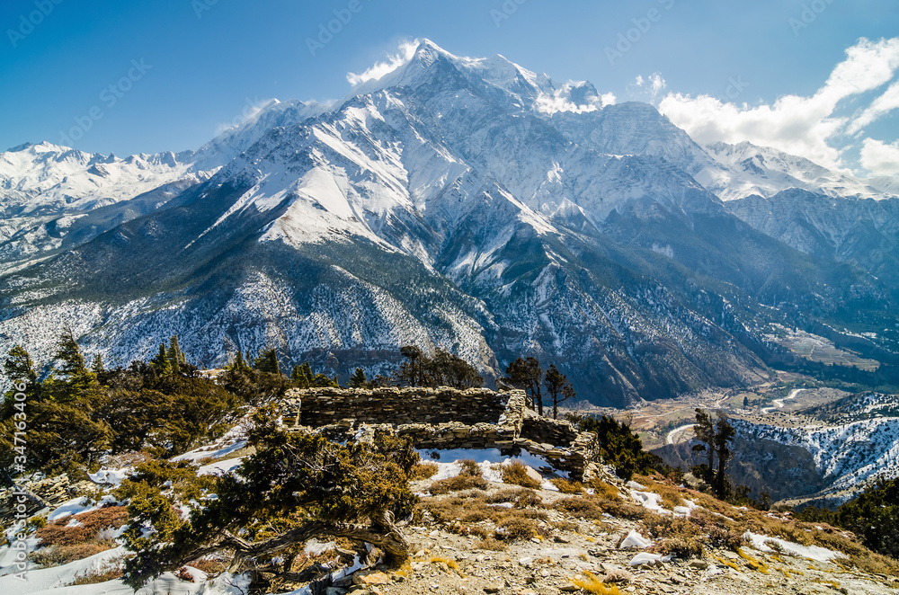 Ruined house on the rocky mountain slope against Mt. Nilgiri in sunny ...