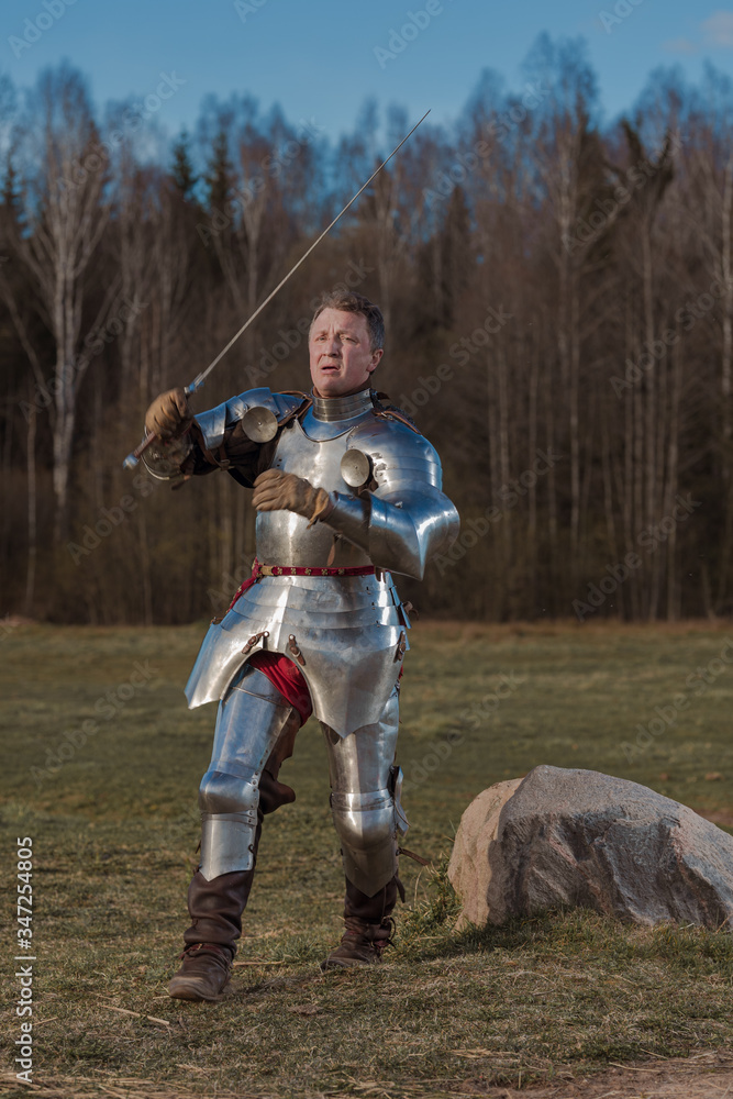 A walking knight in armor and holding a sword in his hands shows combat ...