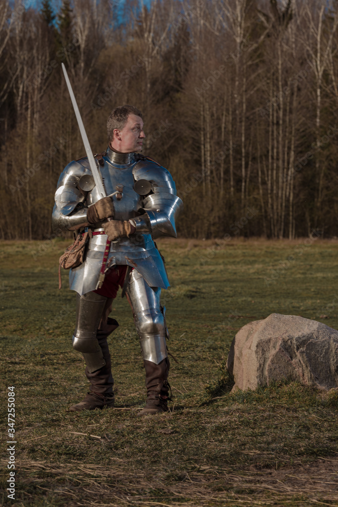 A walking knight in armor and holding a sword in his hands shows combat ...