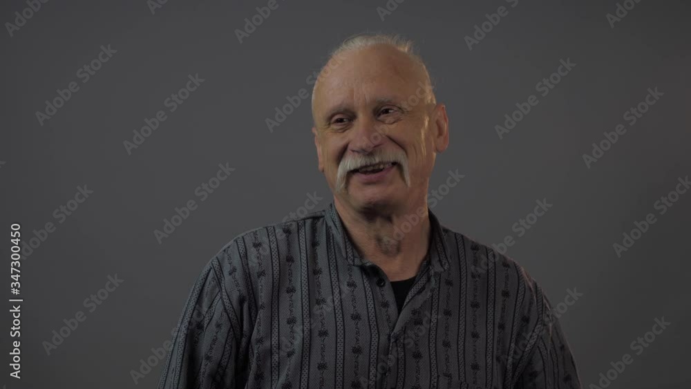 serious angry aged man with grey hair raised eyebrow holds hands on hips and looks forward close ...