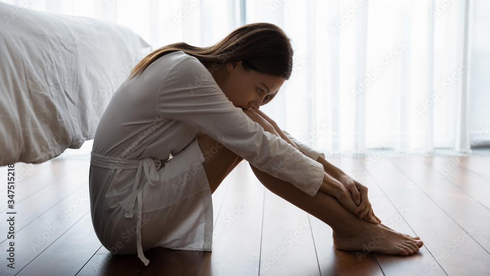 Sad young woman in white nightrobe sit barefoot on floor in bedroom ...