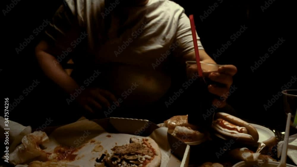Fat man eats junk food and drinks soda, watches TV at home. Gluttony ...