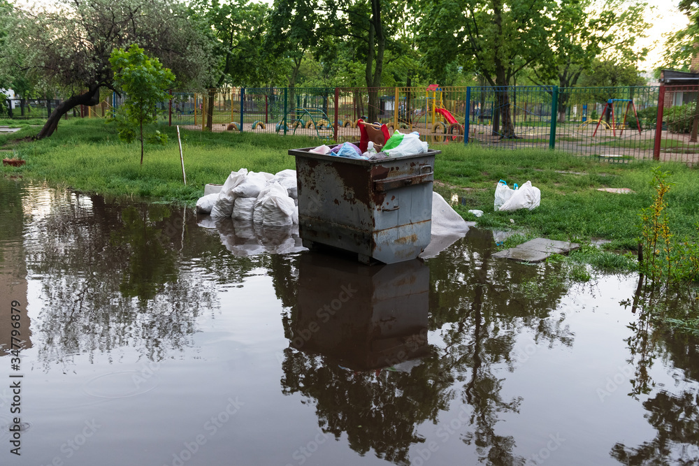 Rain flooded the city. An old metal trash can with rubbish flooded ...