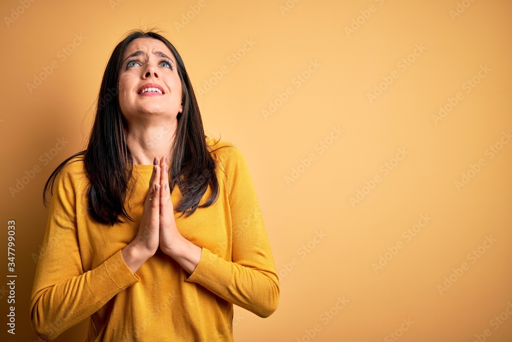 Young brunette woman with blue eyes wearing casual sweater over yellow ...
