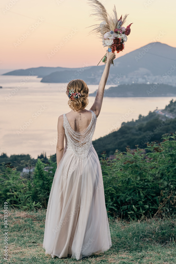 back view of the bride standing on the mountain and raising her hand ...