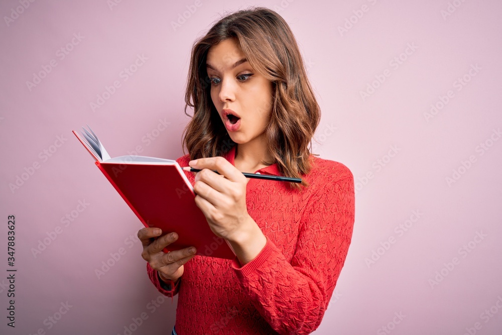 Young blonde student girl reading a book over pink isolated background ...