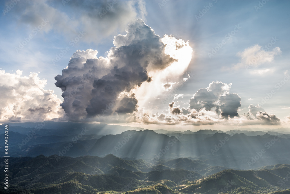 Golden light rays from clouds shining down to mountains. Sun rays over ...