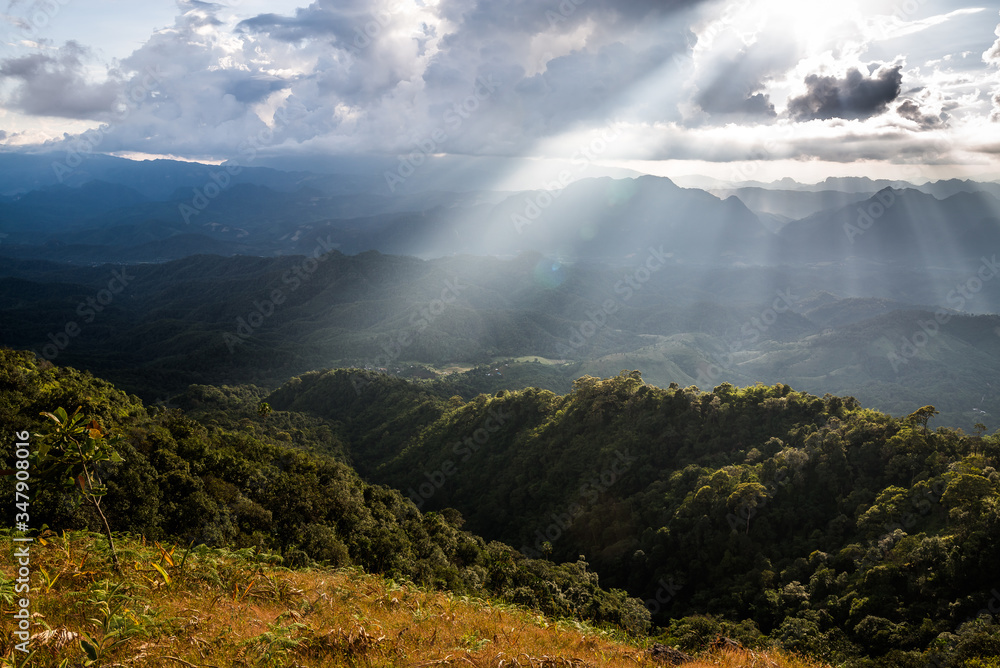 Golden light rays from clouds shining down to mountains. Sun rays over ...