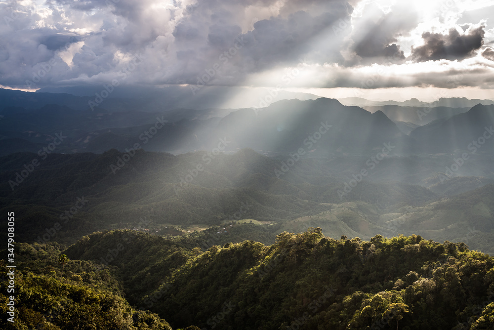Golden light rays from clouds shining down to mountains. Sun rays over ...