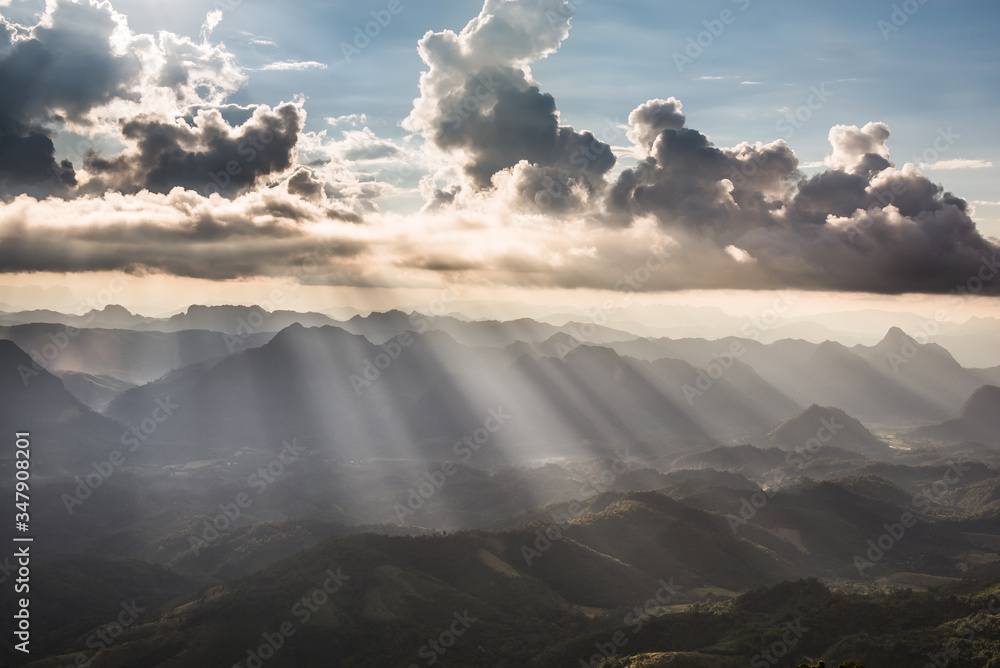 Golden light rays from clouds shining down to mountains. Sun rays over ...