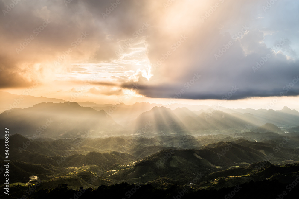 Golden light rays from clouds shining down to mountains. Sun rays over ...