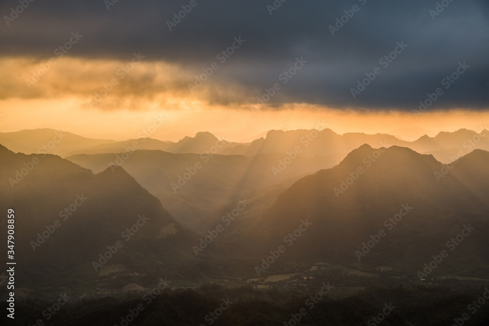Golden light rays from clouds shining down to mountains. Sun rays over ...