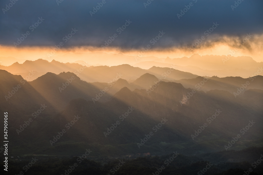 Golden light rays from clouds shining down to mountains. Sun rays over ...