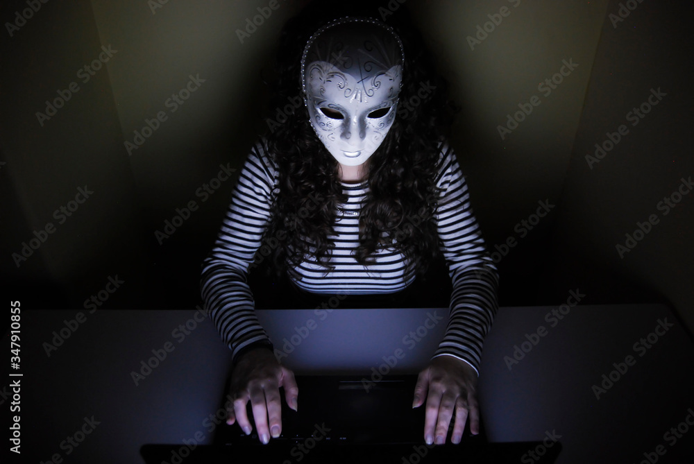 A female hacker typing in a keyboard on a laptop wearing a mask ...