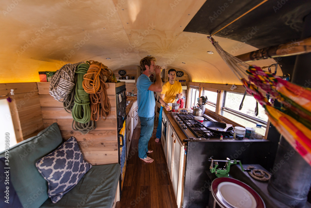 two people drinking beverage inside converted school bus with ropes ...