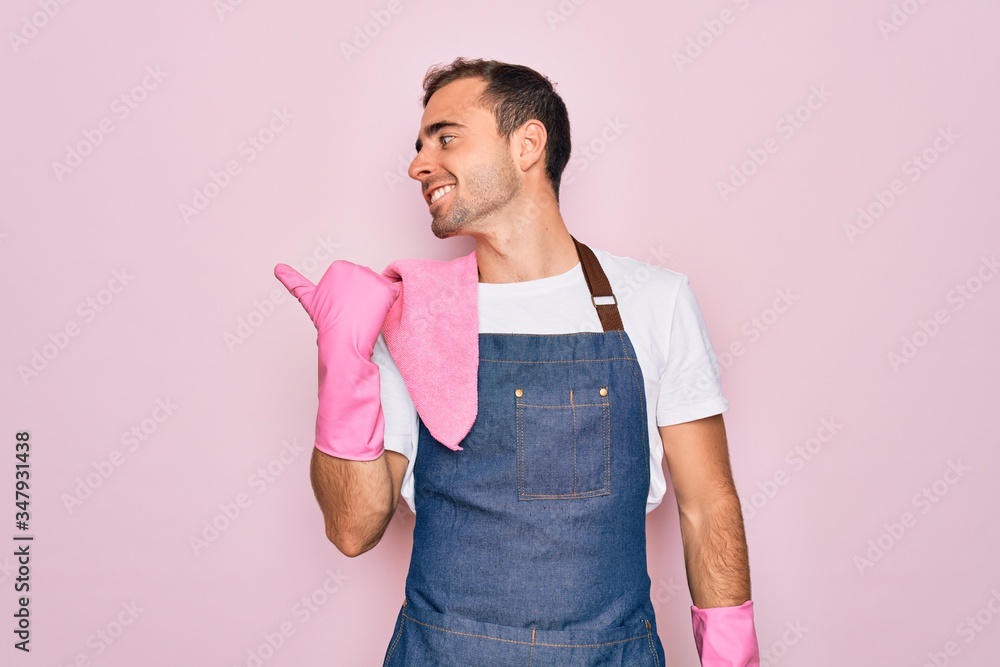 Young cleaner man with blue eyes cleaning wearing apron and gloves over ...