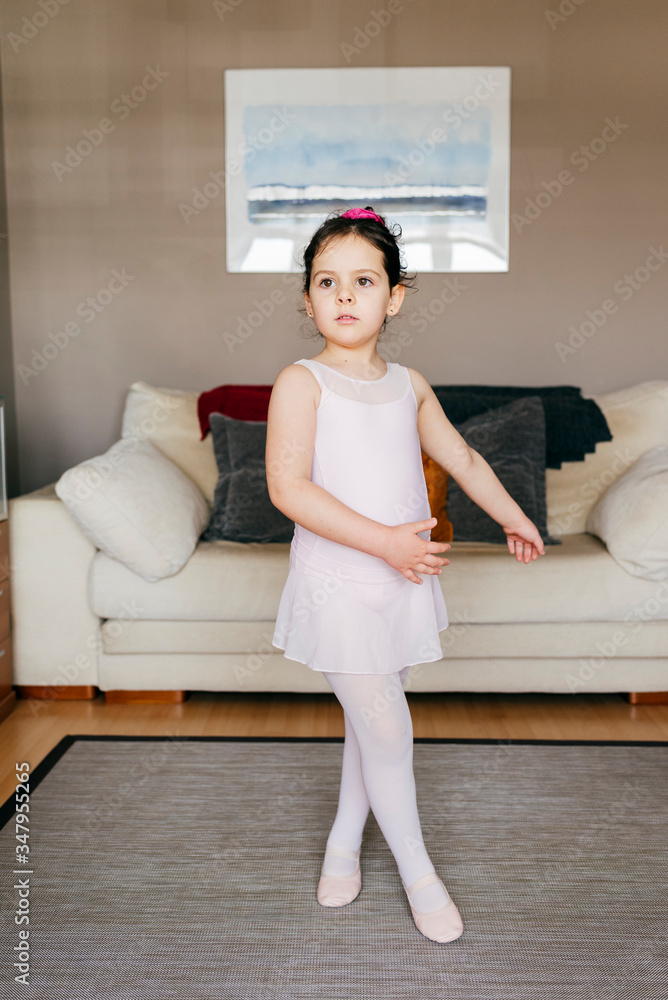 Cute little girl looking away dancing near sofa during ballet rehearsal ...