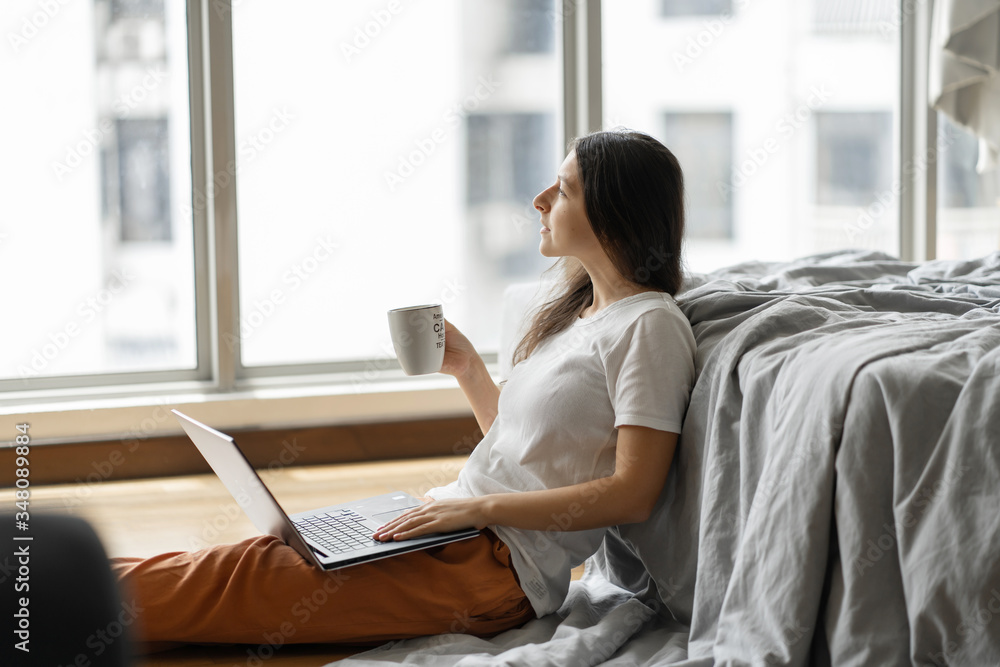 Beautiful young brunette girl working on a laptop and drinking coffee ...