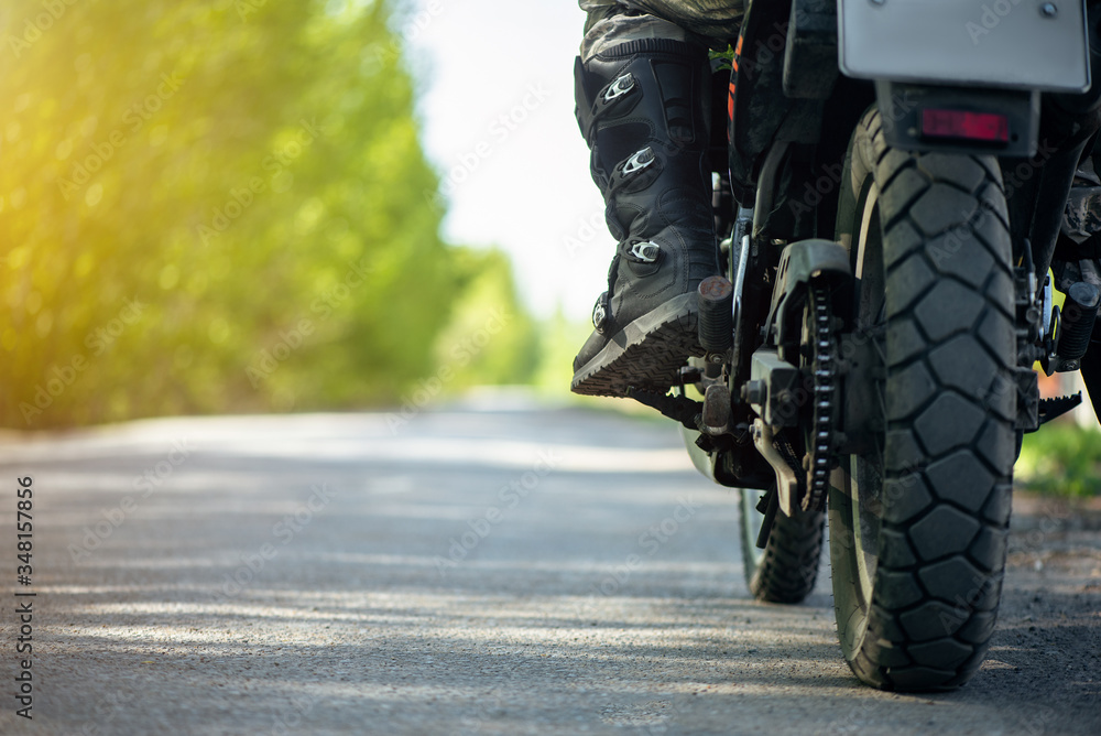 Motorbike wheel and biker leg in the boot close up on empty road ...