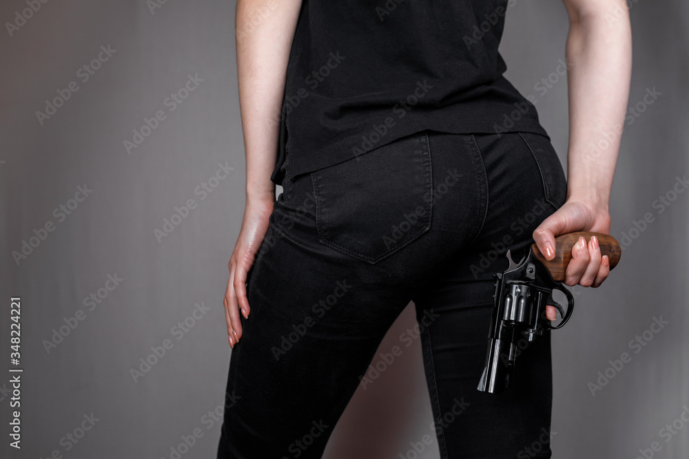 Armed girl in black jeans hides her pistols gun behind her back. Hidden ...